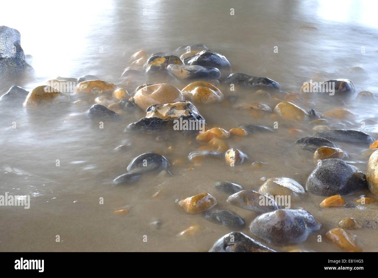 Pebbles on a beach with the sea washing over them Stock Photo - Alamy