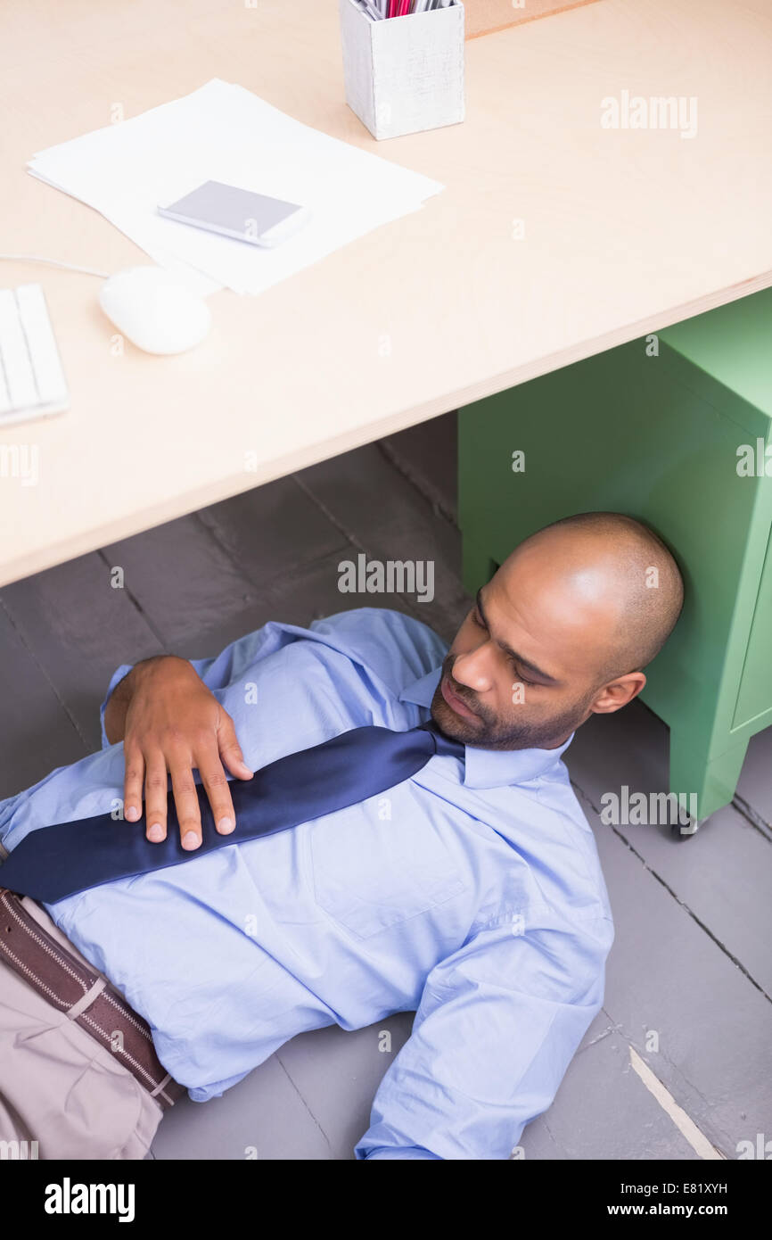 Businessman sleeping under desk Stock Photo - Alamy