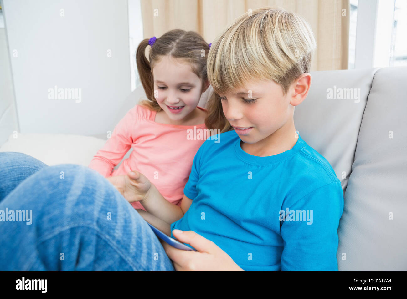 Happy siblings using tablet pc on sofa Stock Photo - Alamy