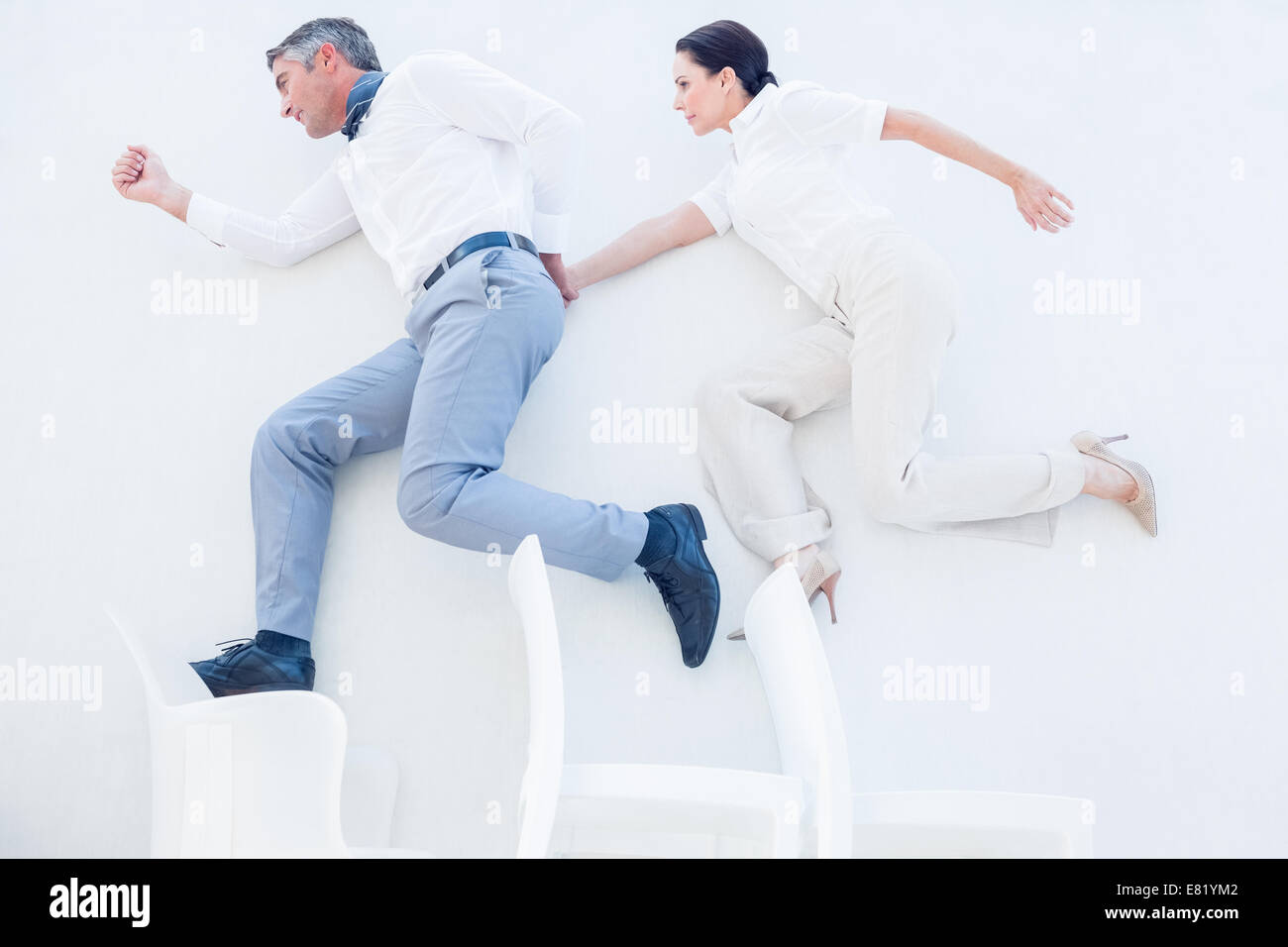 Business partners jumping over chairs Stock Photo - Alamy