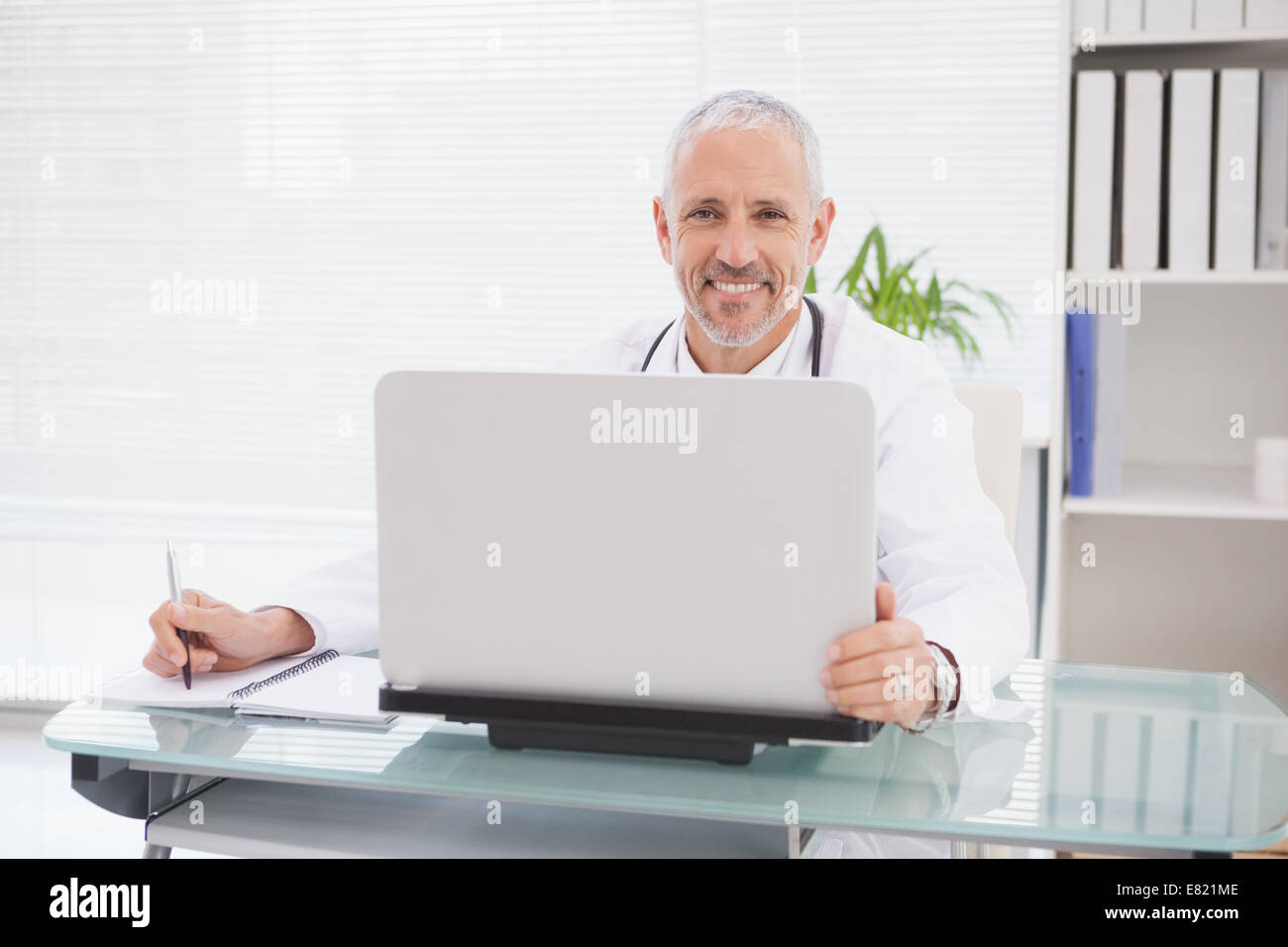 Smiling doctor using laptop and writing Stock Photo - Alamy