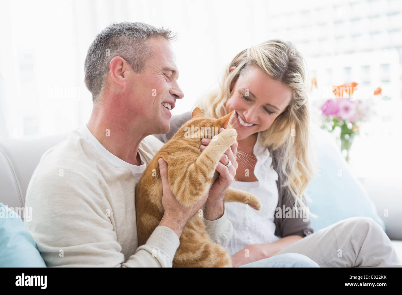 Smiling couple petting their gringer cat on the couch Stock Photo - Alamy