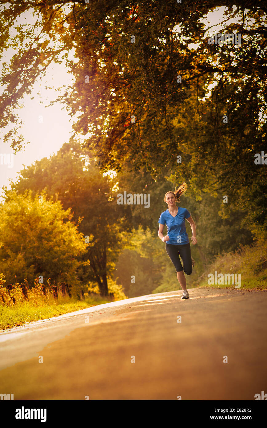 Sporty woman running on a country road approaching the camera as she ...