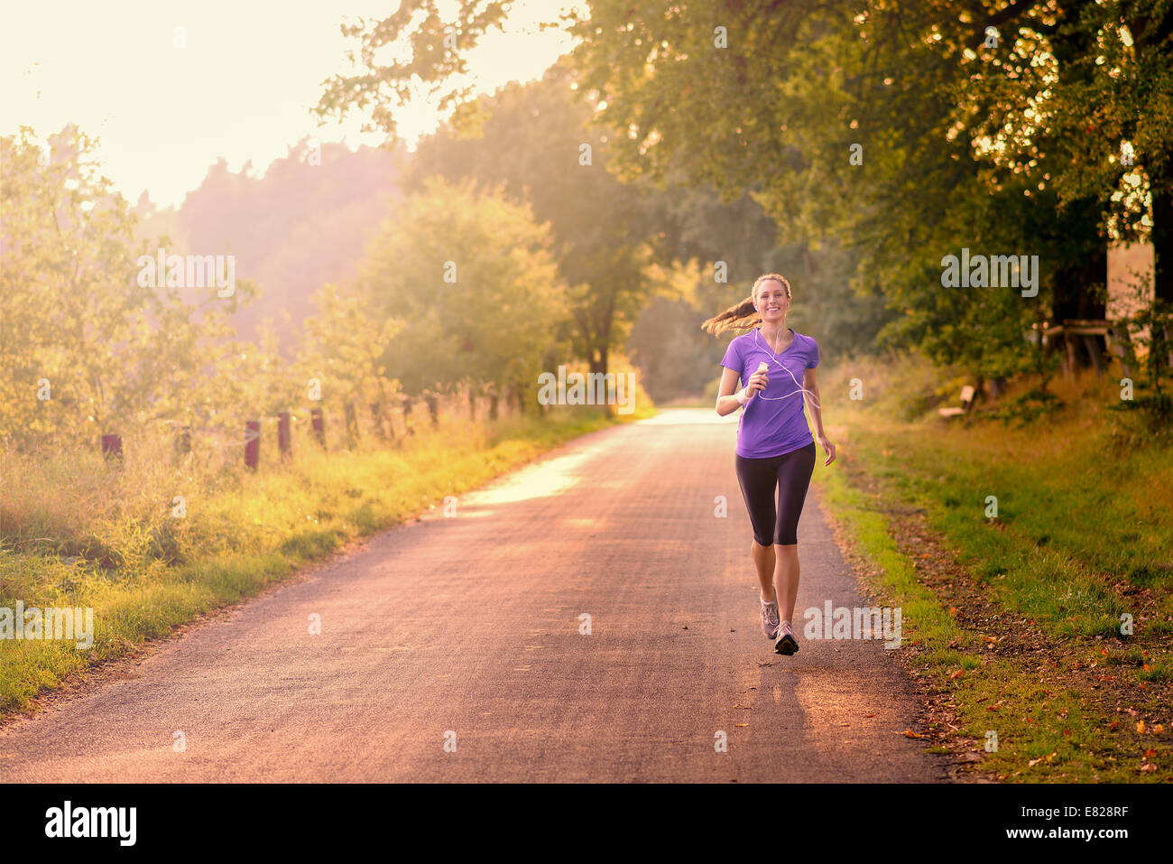 Sporty woman running on a country road approaching the camera as she ...