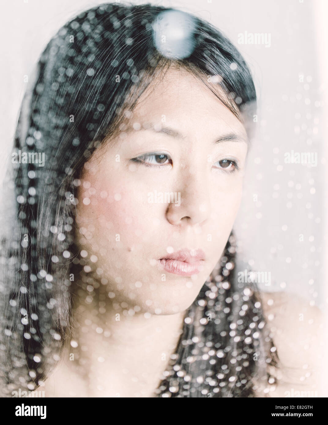 Young woman looking through a window with water drops Stock Photo - Alamy