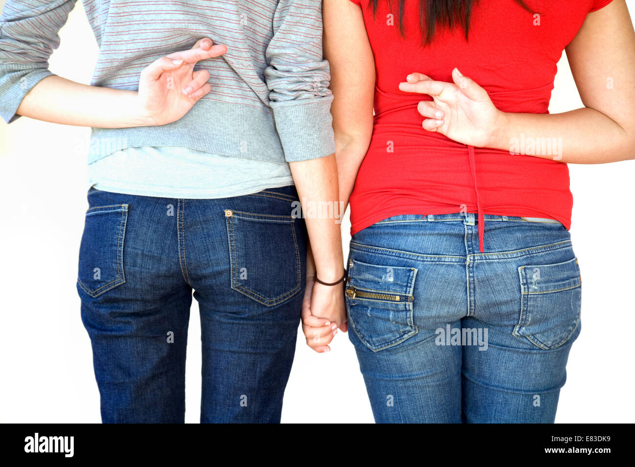 Two teenage girls standing holding hands with fingers crossed behind ...