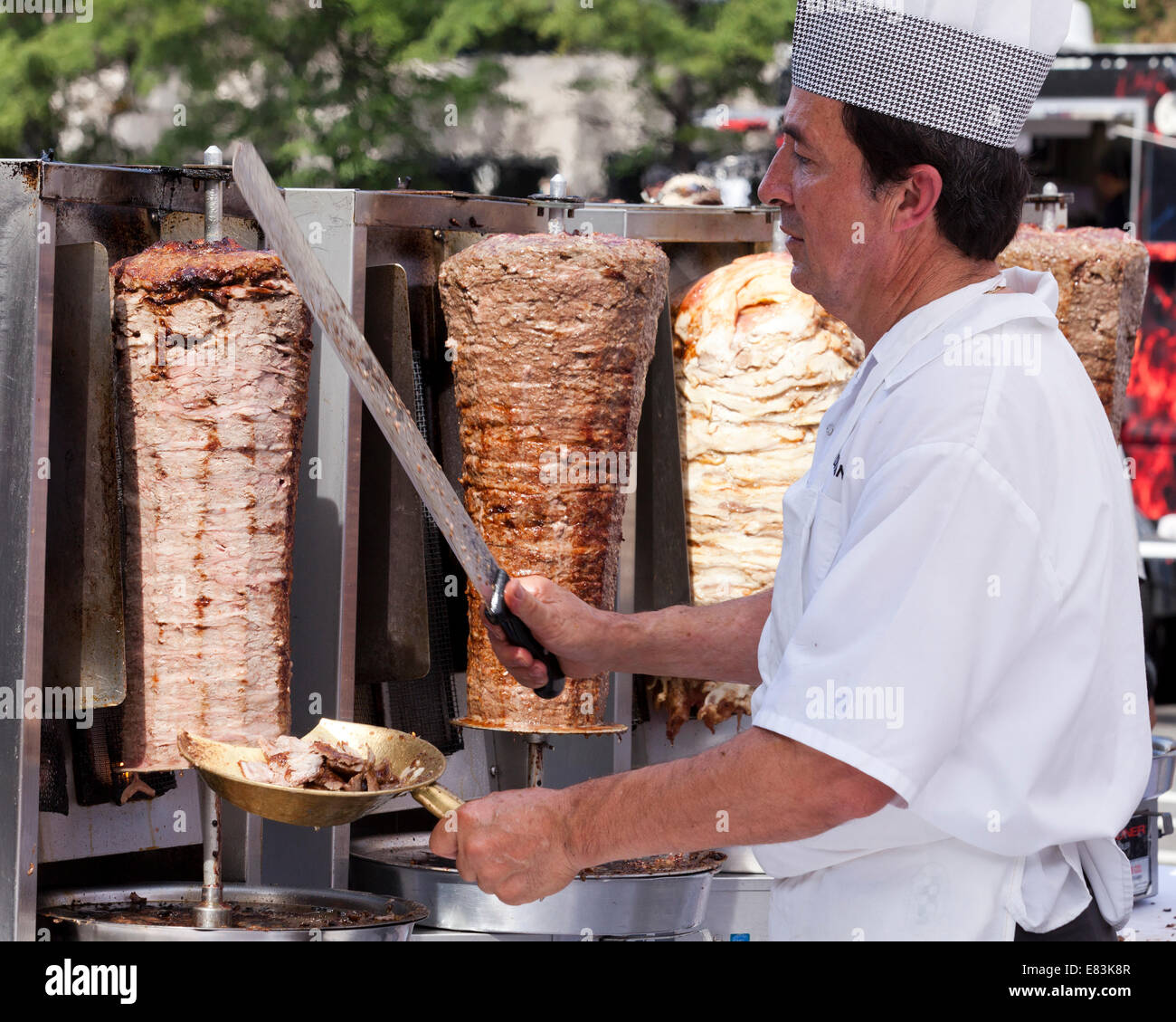 Turkish cook slicing Doner kebab meat from spit at an outdoor festival ...