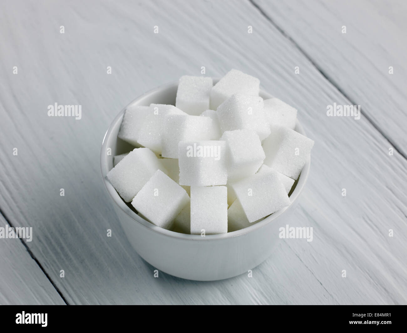 a white bowl of sugar cubes or lumps on a wooden surface Stock Photo ...