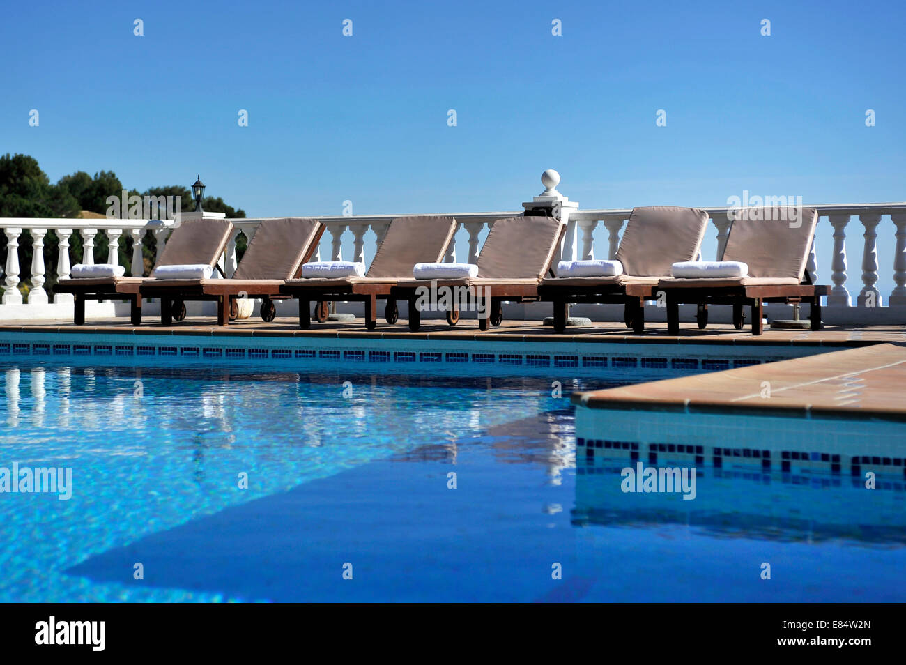 six sun loungers by the side of a swimming pool in the sun and blue sky ...