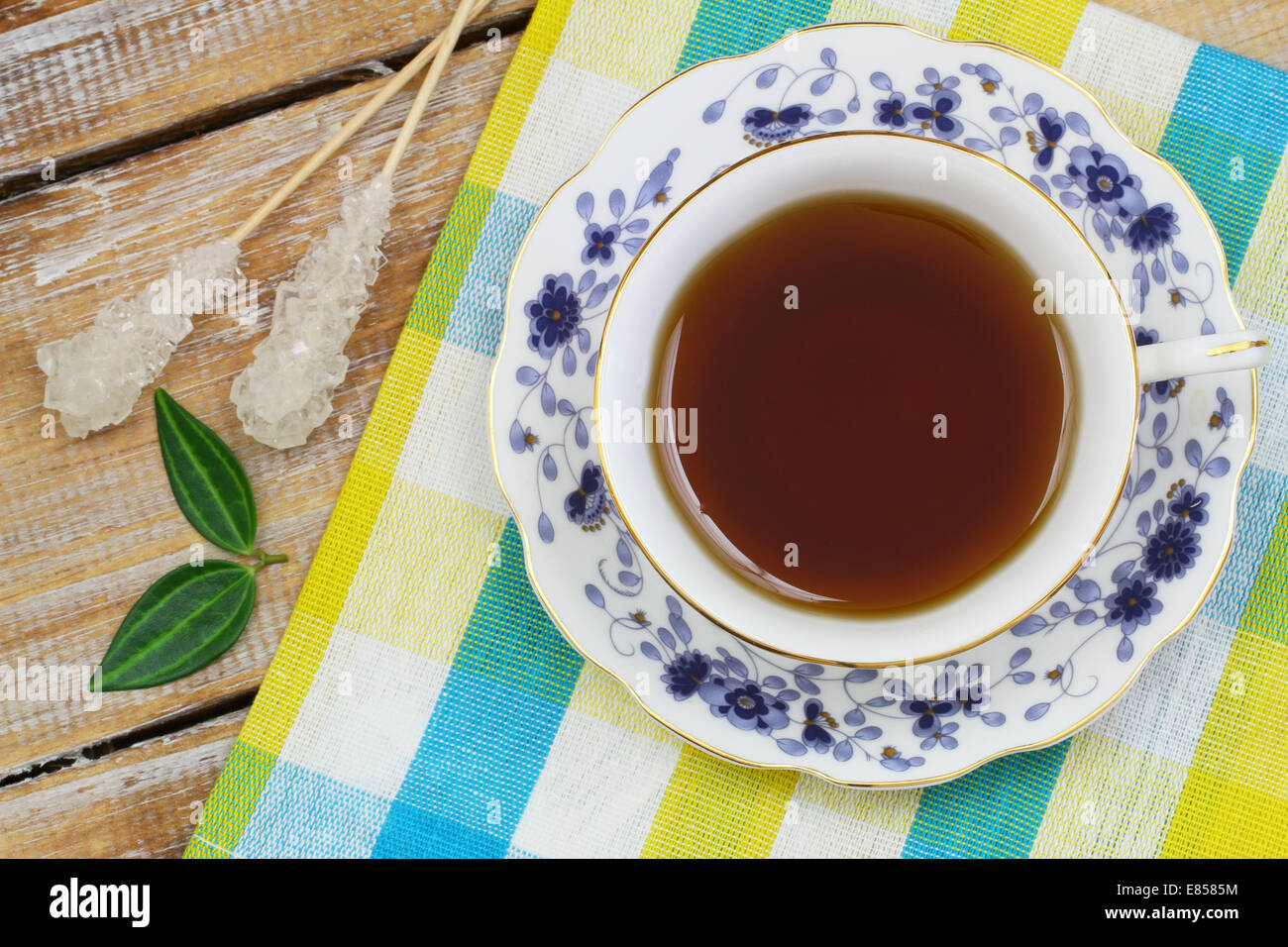 Black tea in vintage cup, sugar sticks on colorful cloth on wooden ...