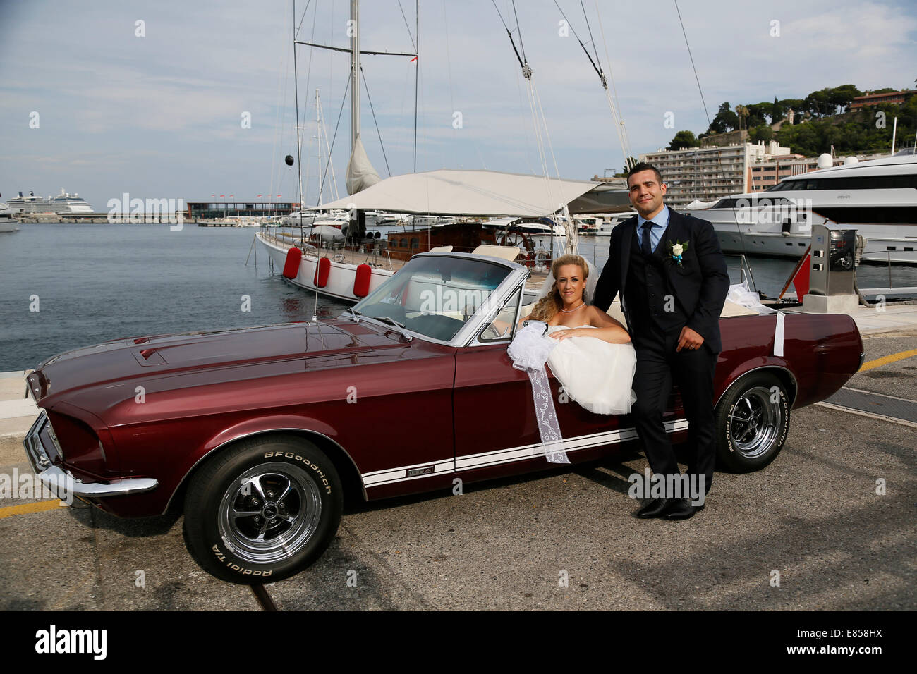 Bride and groom posing with an open Ford Mustang convertible car at a ...