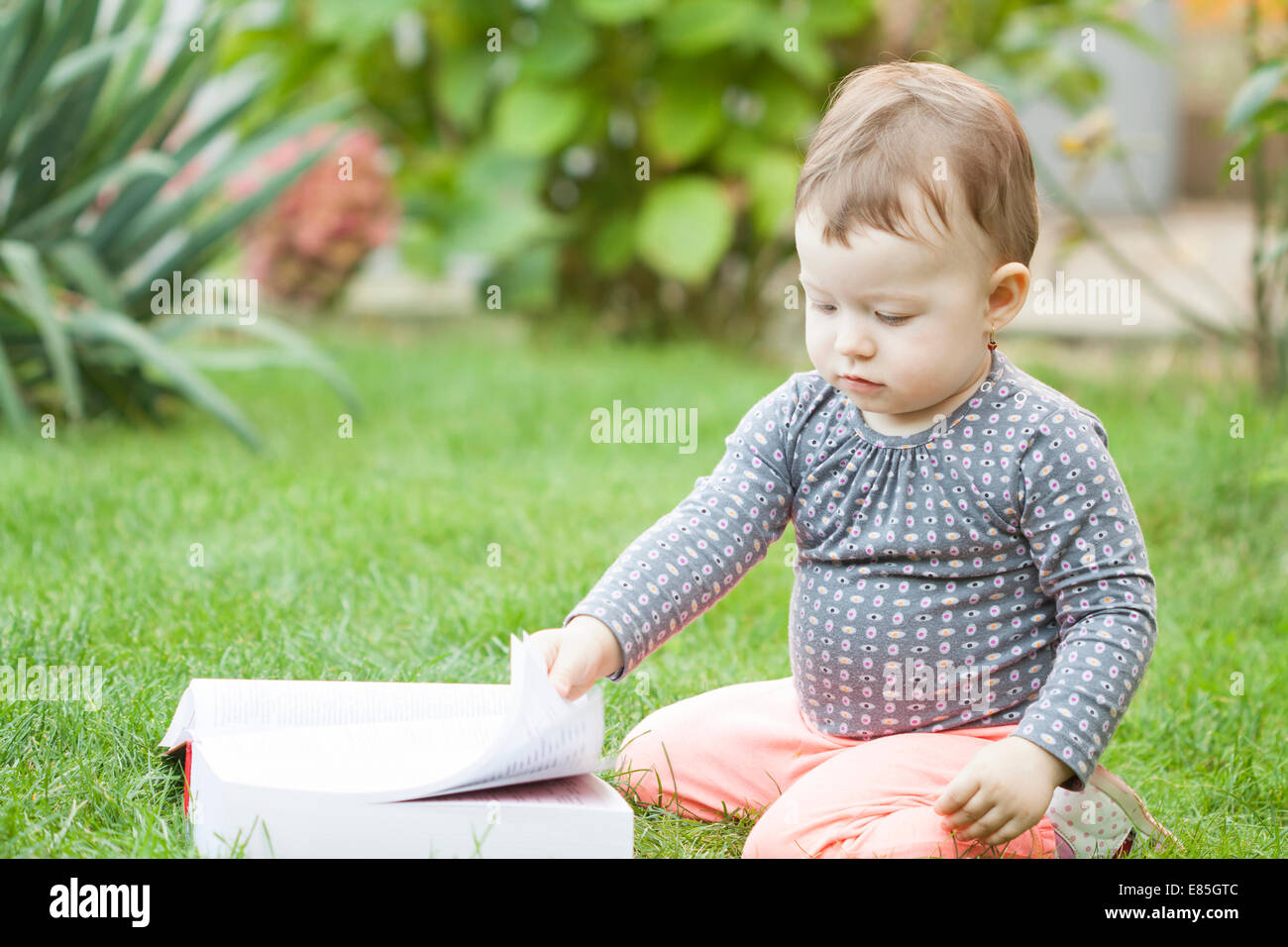 Baby girl looking at a book in the park Stock Photo - Alamy