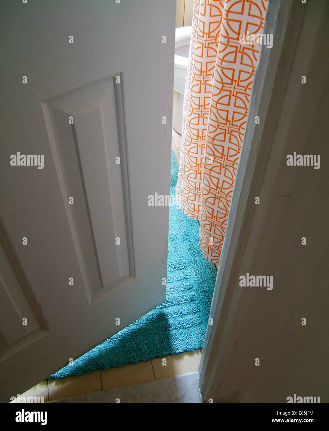 View through narrowly open door onto a blue rug and orange detailed ...