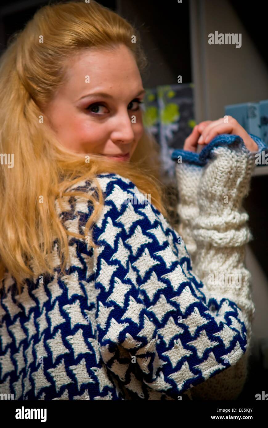 Blonde woman stands at bookcase in patterned jacket Stock Photo - Alamy
