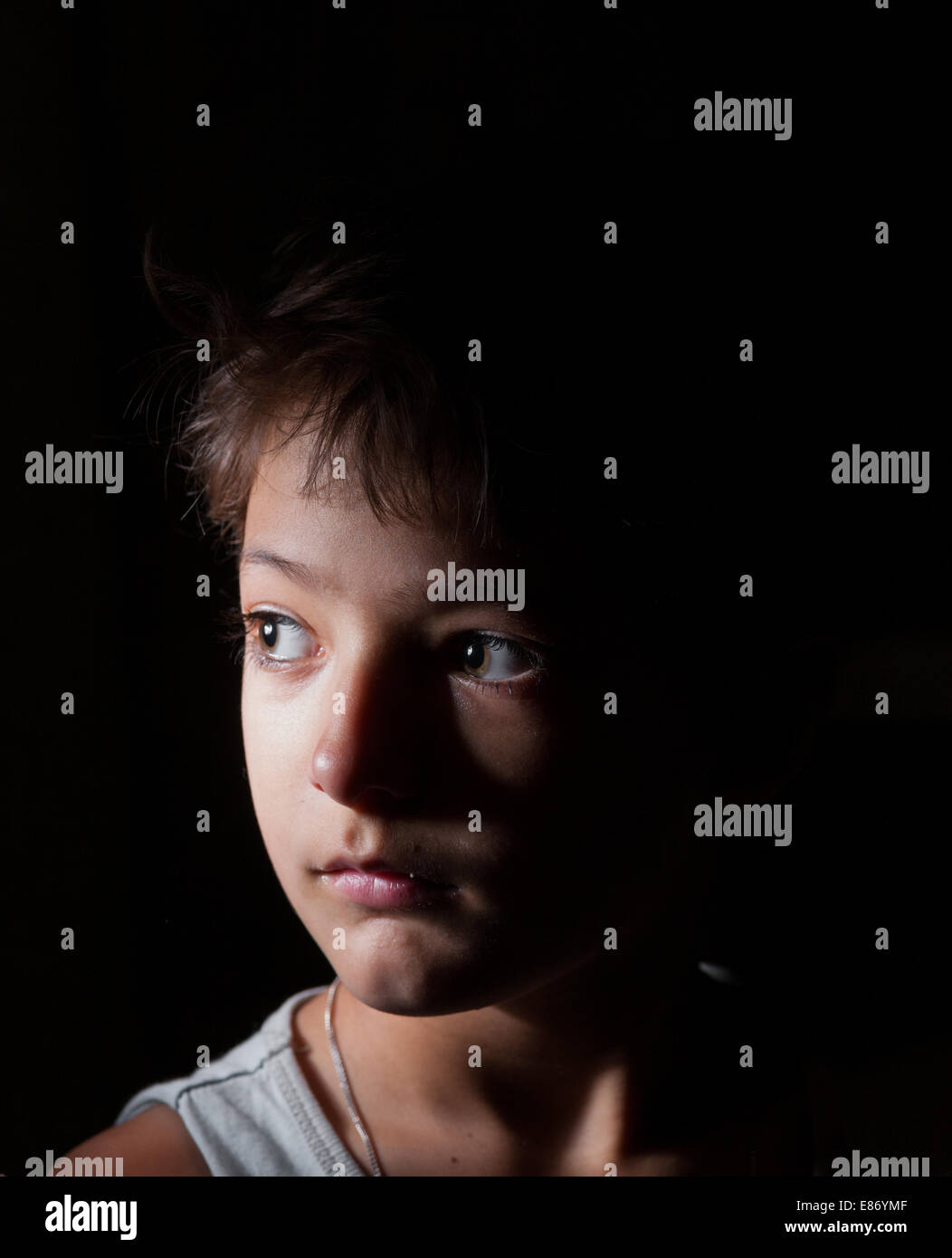 sad boy in the dark, focused light on the one side, looking away ...