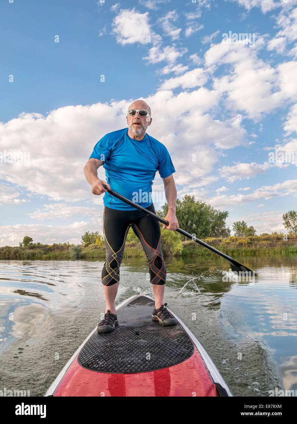 senior male paddler paddling a stand up paddleboard (SUP), calm lake in ...