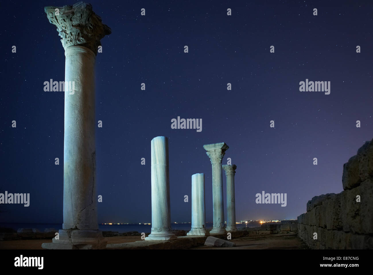 Ruins of ancient city columns under blue night sky with moon and stars ...