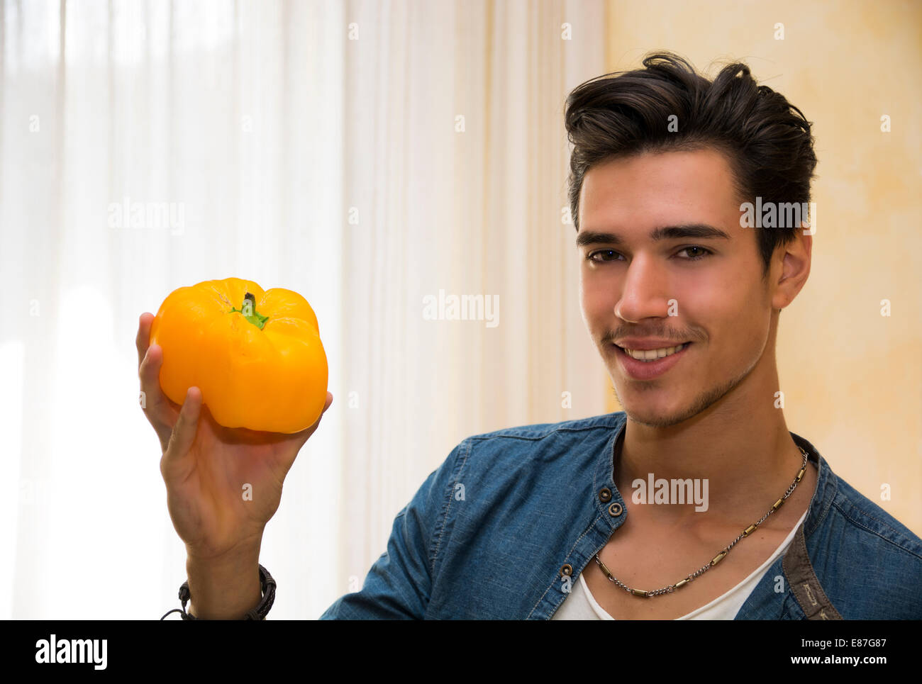 Smiling young man holding a fresh yellow pepper or capsicum in his hand ...