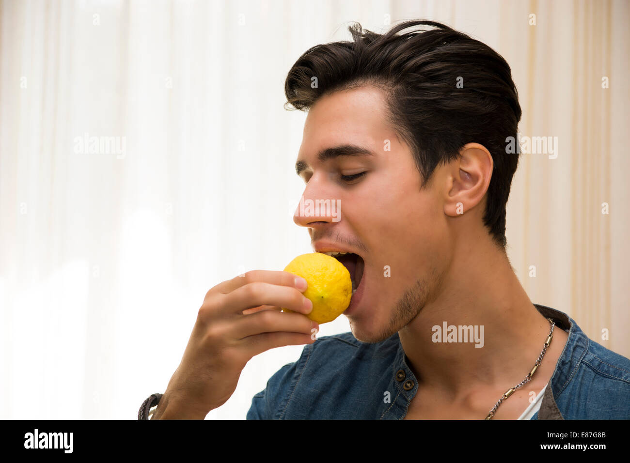Headshot of handsome young man biting lemon Stock Photo - Alamy