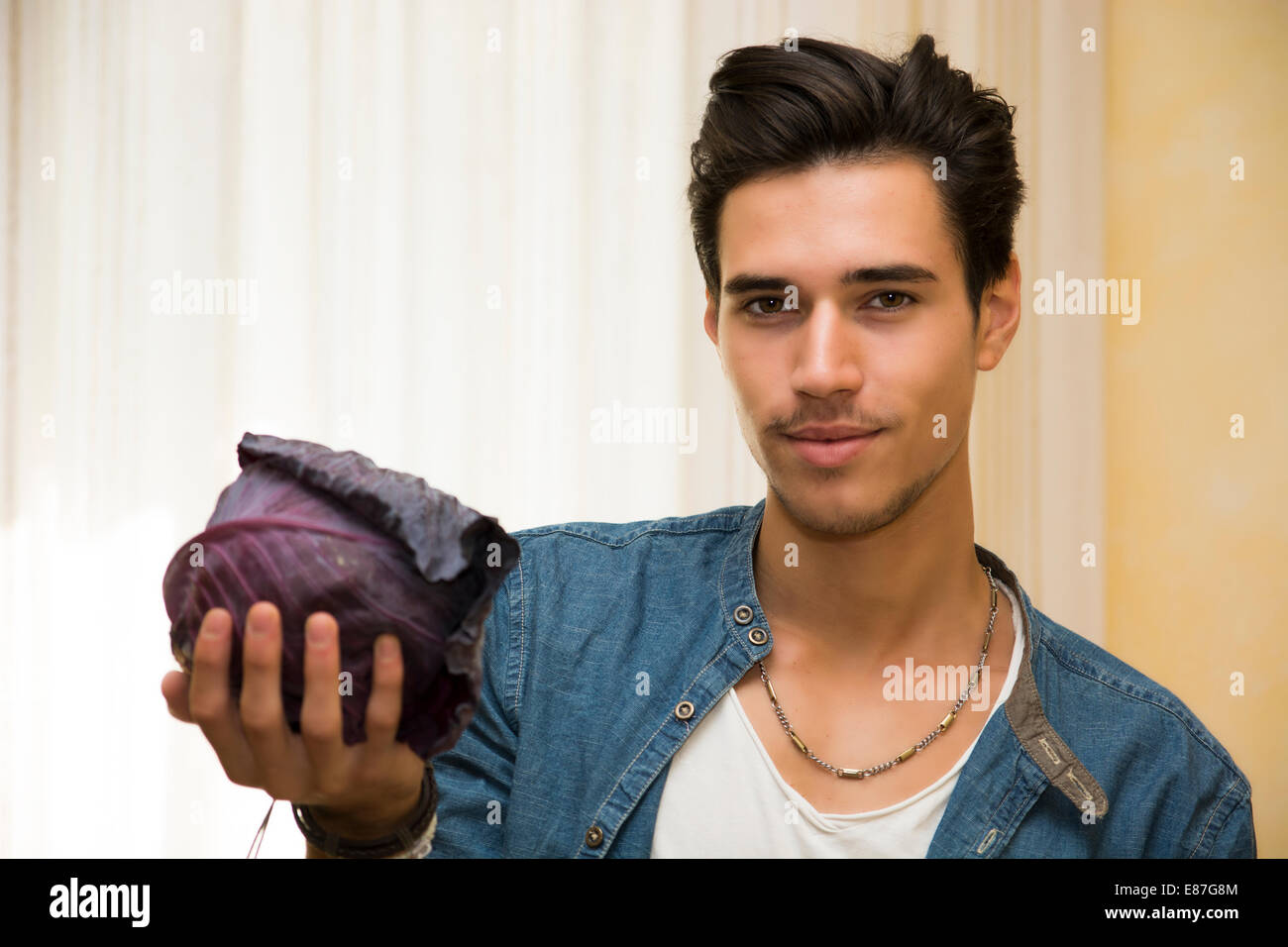Smiling young man holding a fresh black cabbage in his hand in a ...