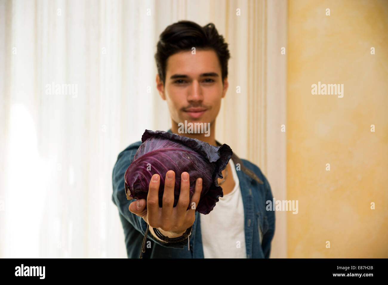 Smiling young man holding a fresh black cabbage in his hand in a ...