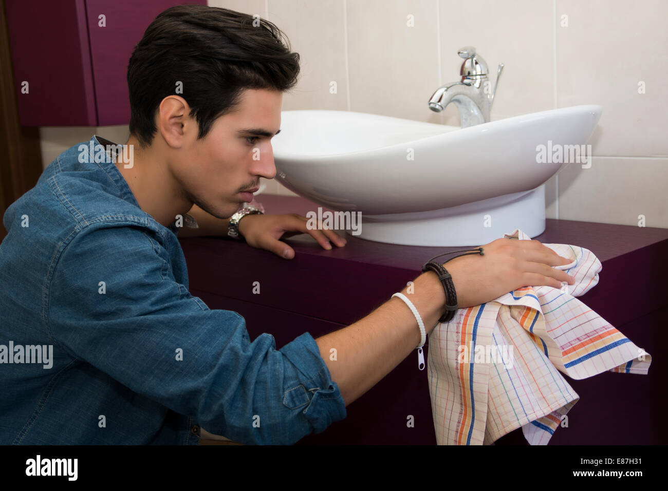 Handsome young man kneeling down with a cloth in his hand cleaning the ...