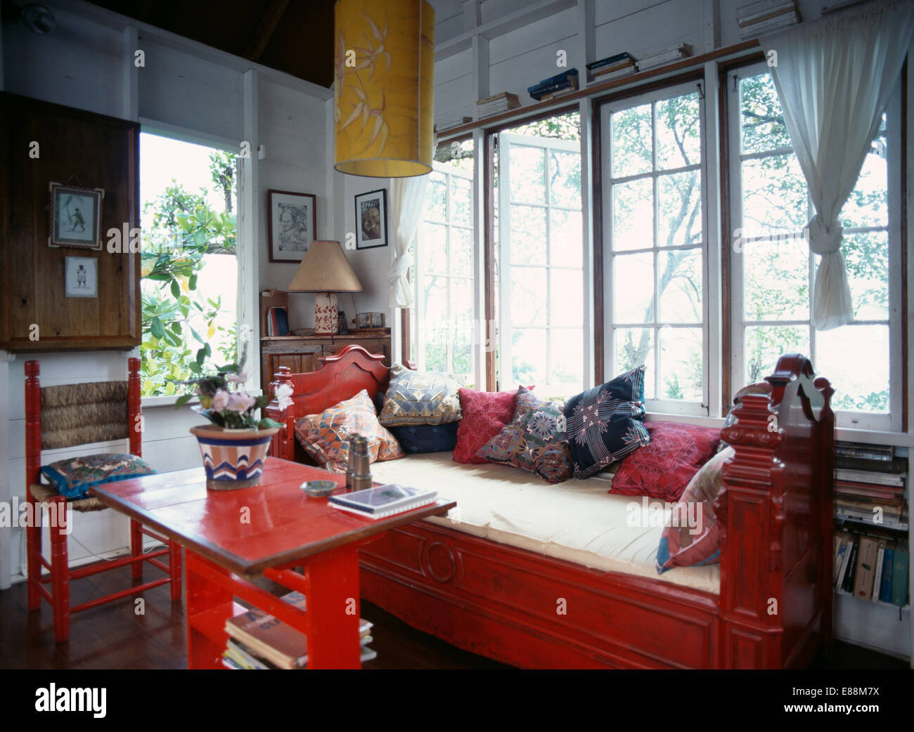 Silk cushions on carved divan below window in small Caribbean living ...