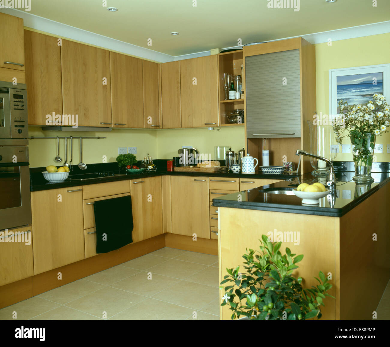 Pale wood units and tambour shutter in modern yellow kitchen with ...