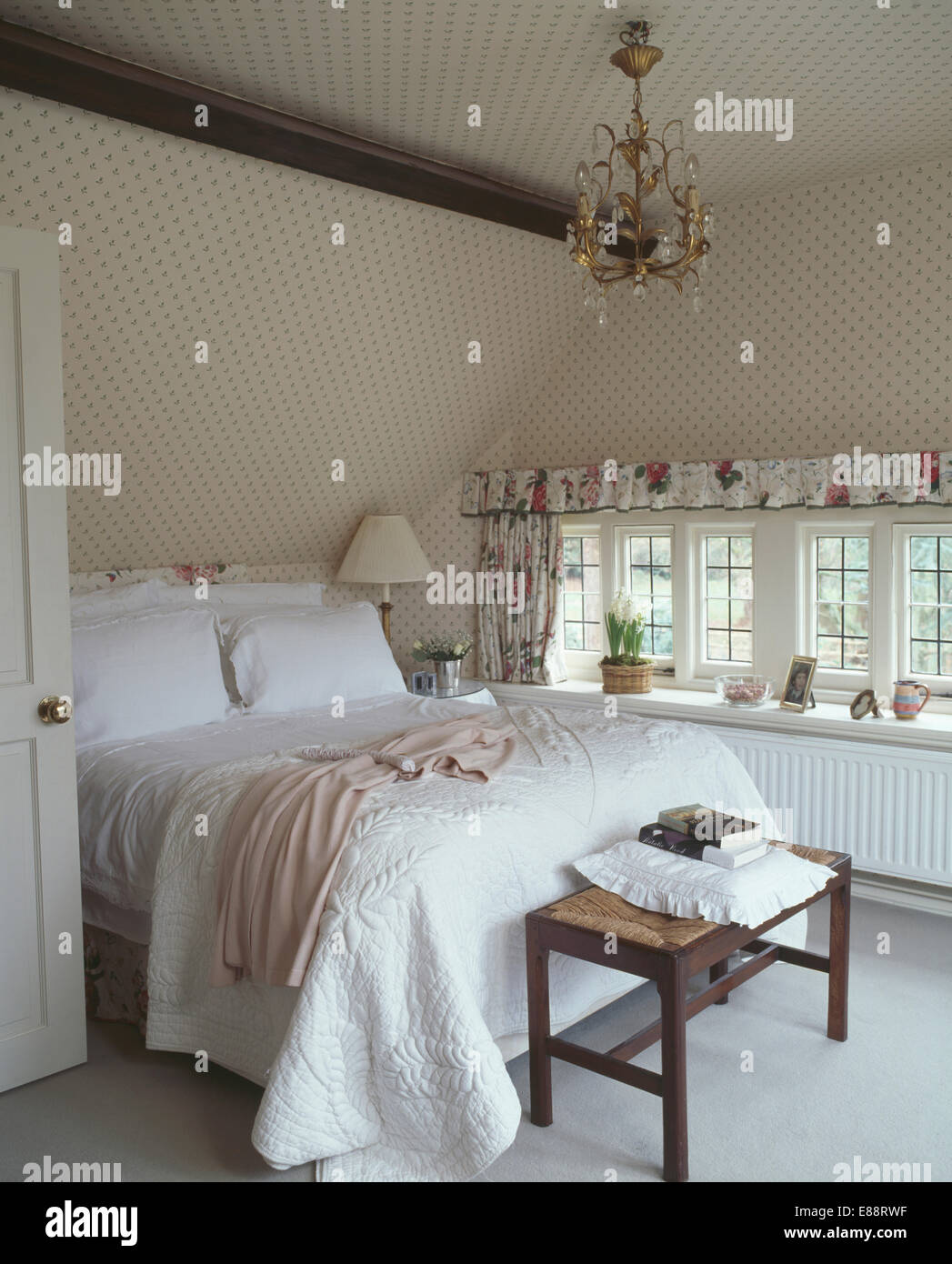 Chandelier above bed with white quilt in attic country bedroom with ...