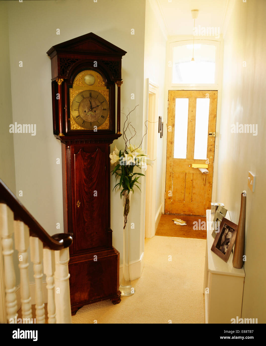 Antique longcase clock in narrow townhouse hall ith white lilies in ...