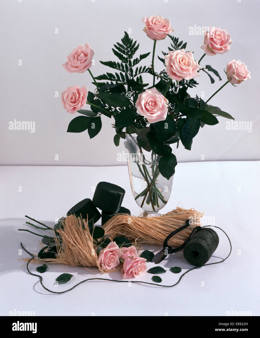 Close-up of vase of pink roses on table with raffia and green string ...