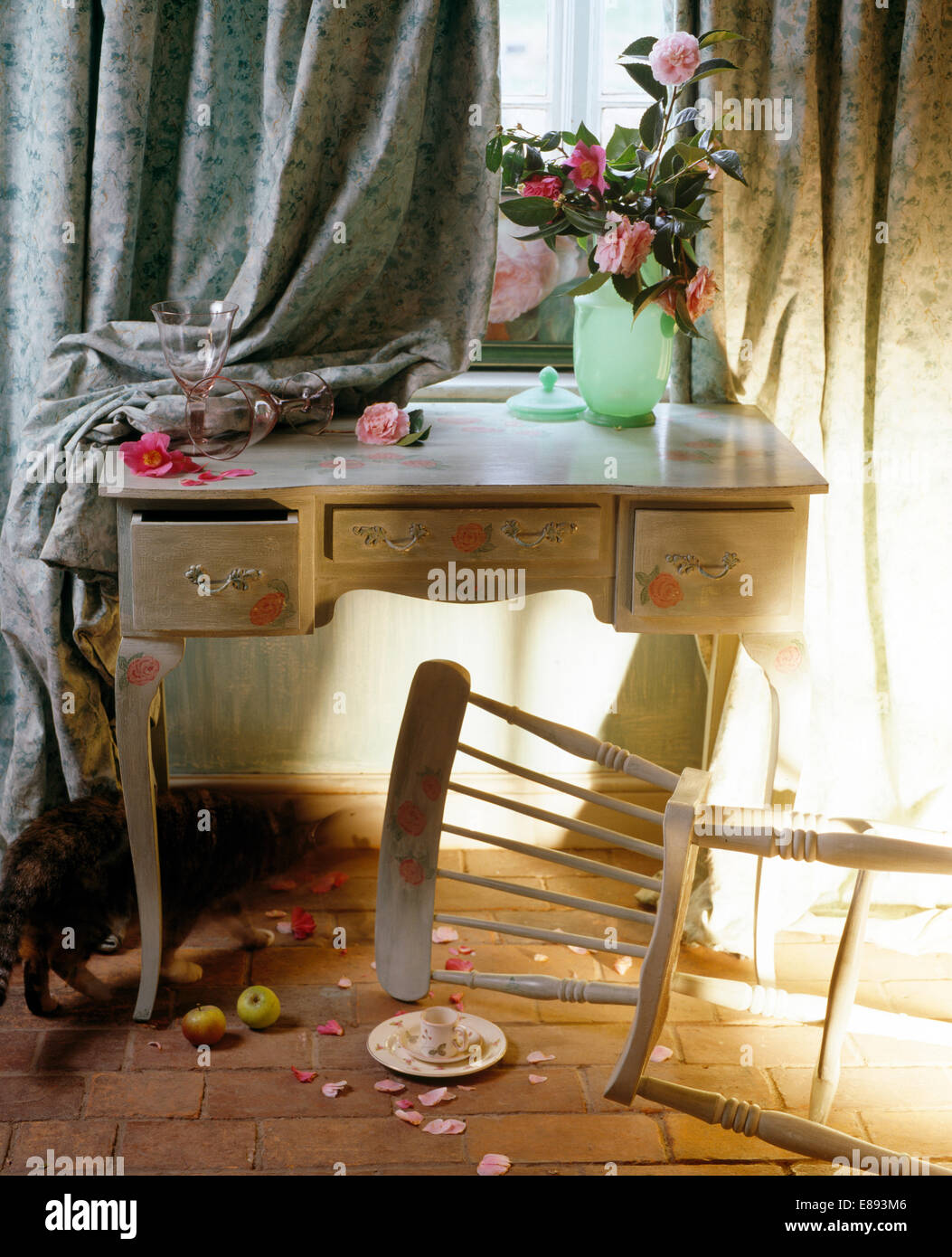Tipped up chair on floor beside painted table with pot of pink roses in ...