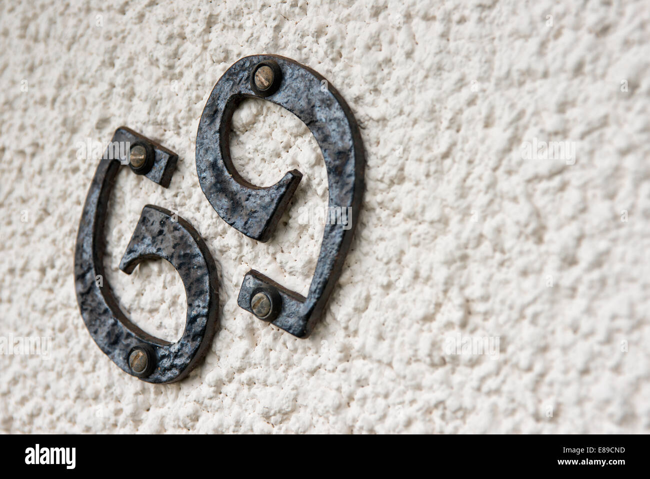 A wrought iron number 69 on a white stucco wall, used to identify the ...