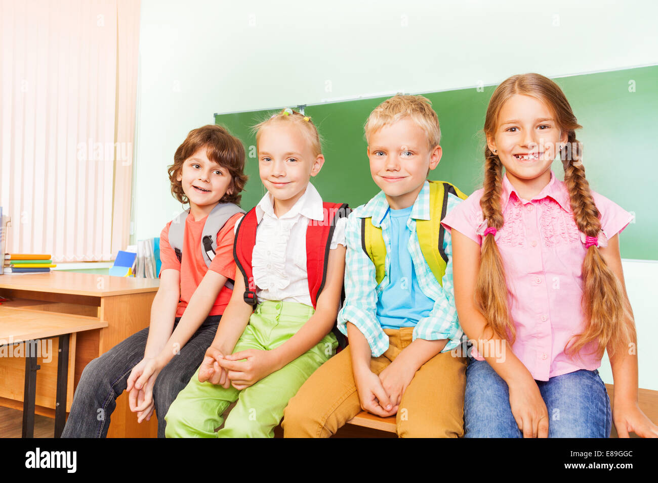 Four schoolchildren sitting in row and smiling Stock Photo - Alamy