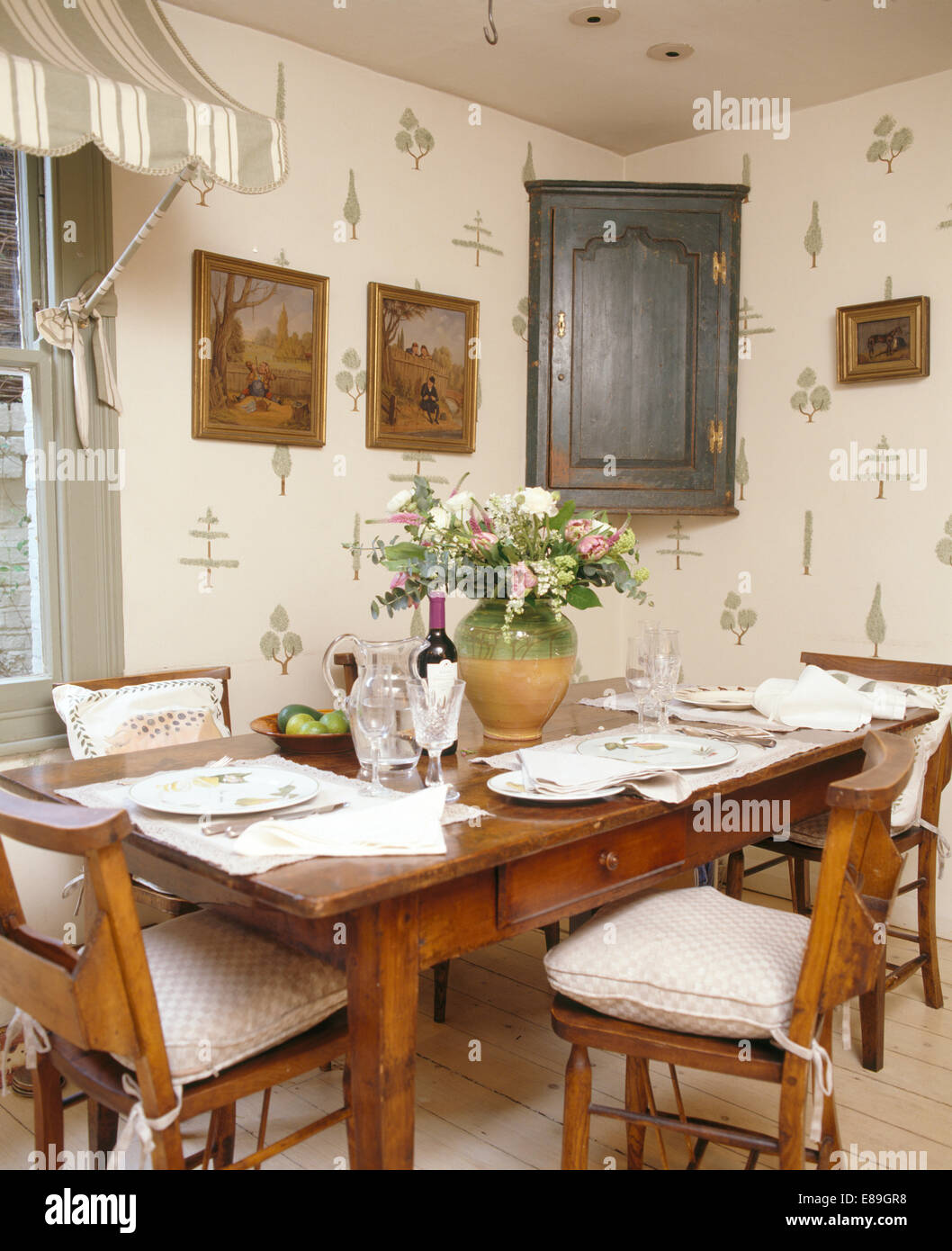 Patterned wallpaper and old chapel chairs at simple wood table set for ...