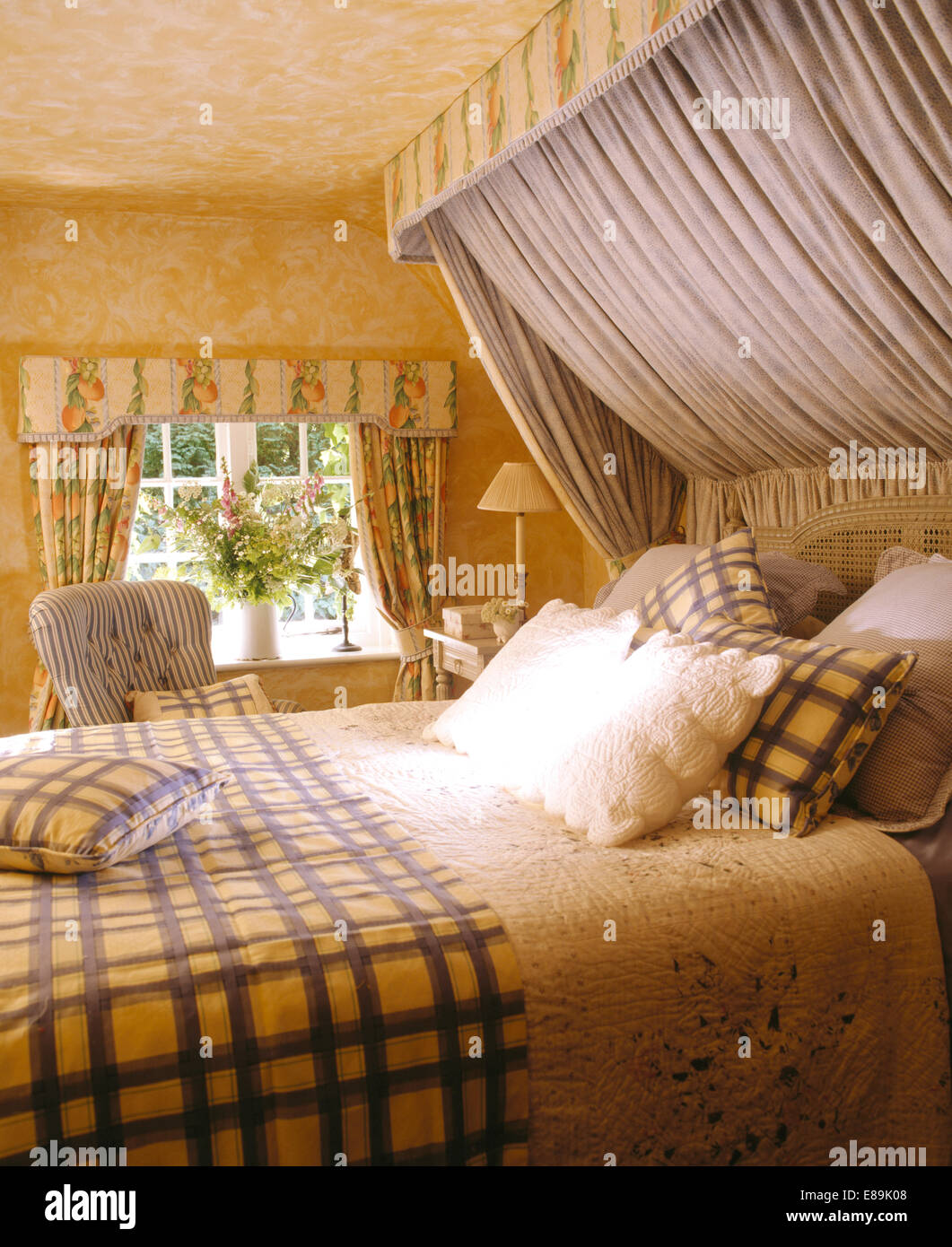 Pale blue drapes and checked bedcover on half-tester bed in country ...