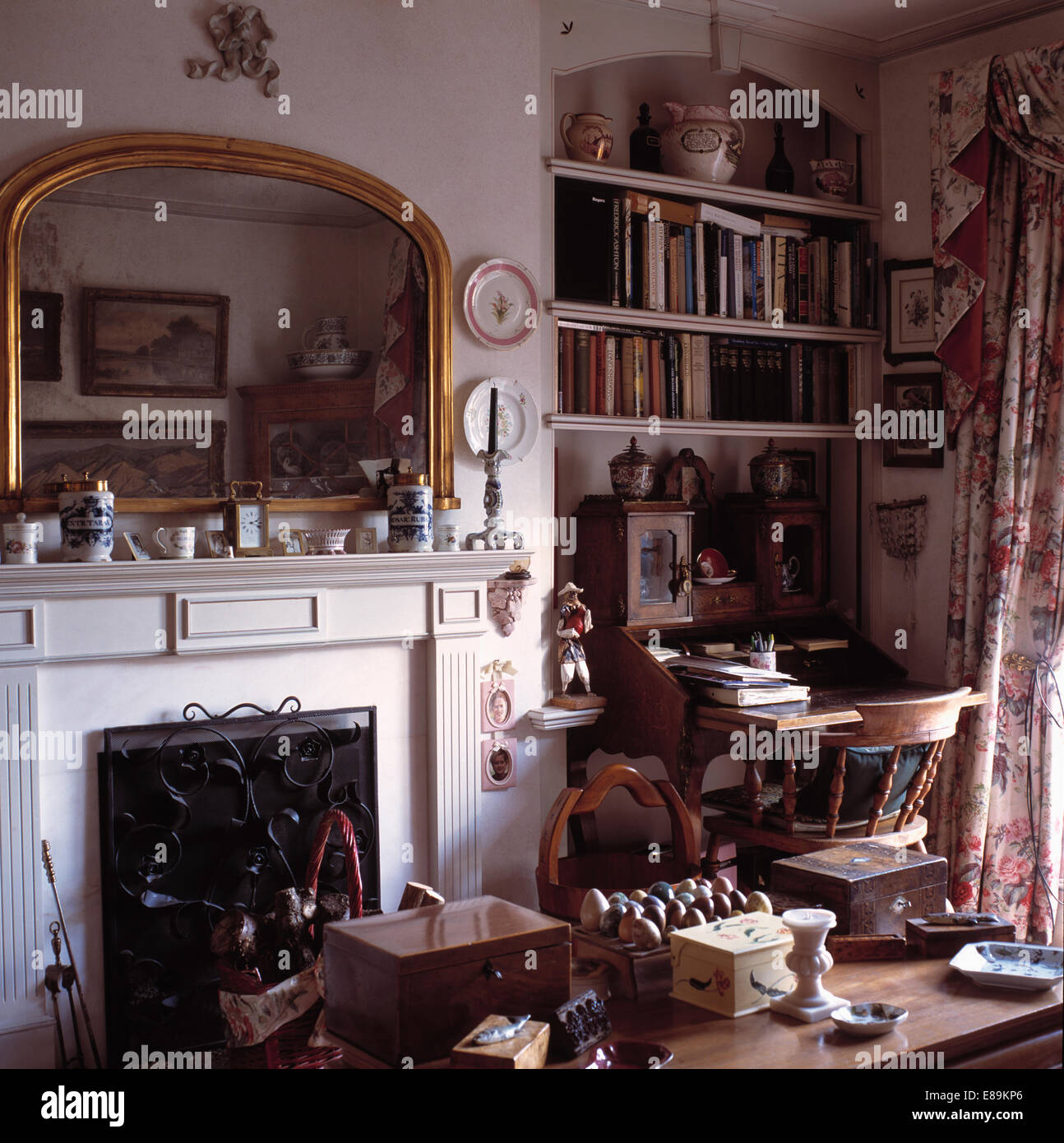 Gilt mirror above fireplace in study with bookshelves above antique ...