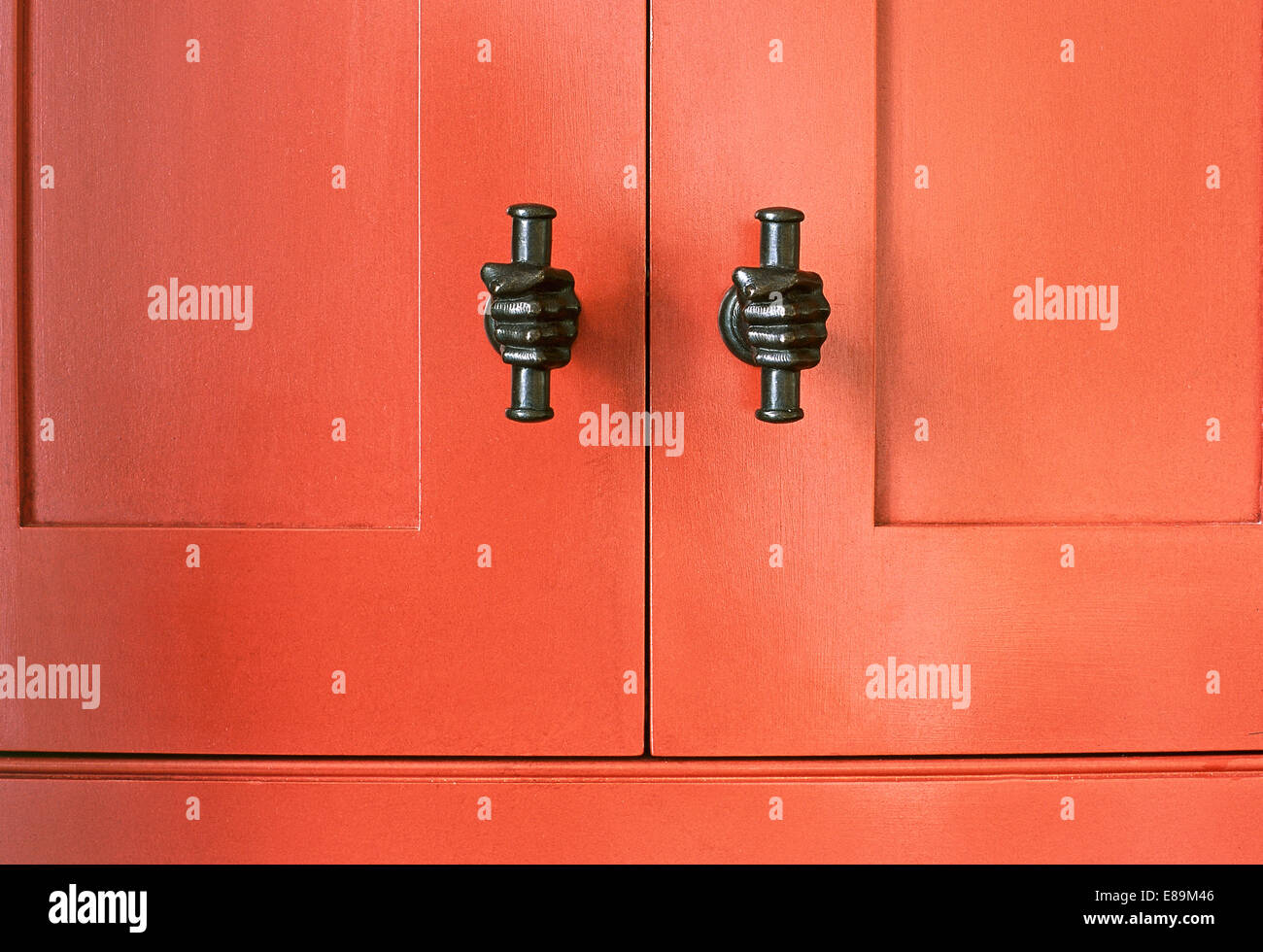 A detail of red painted kitchen cupboards with black metal handles in ...
