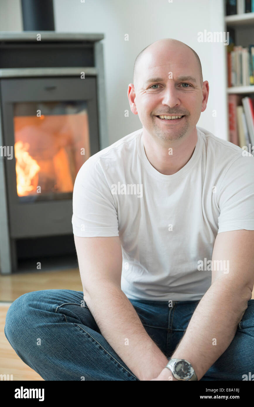 Portrait of man sitting in his living room with fireplace, smiling ...