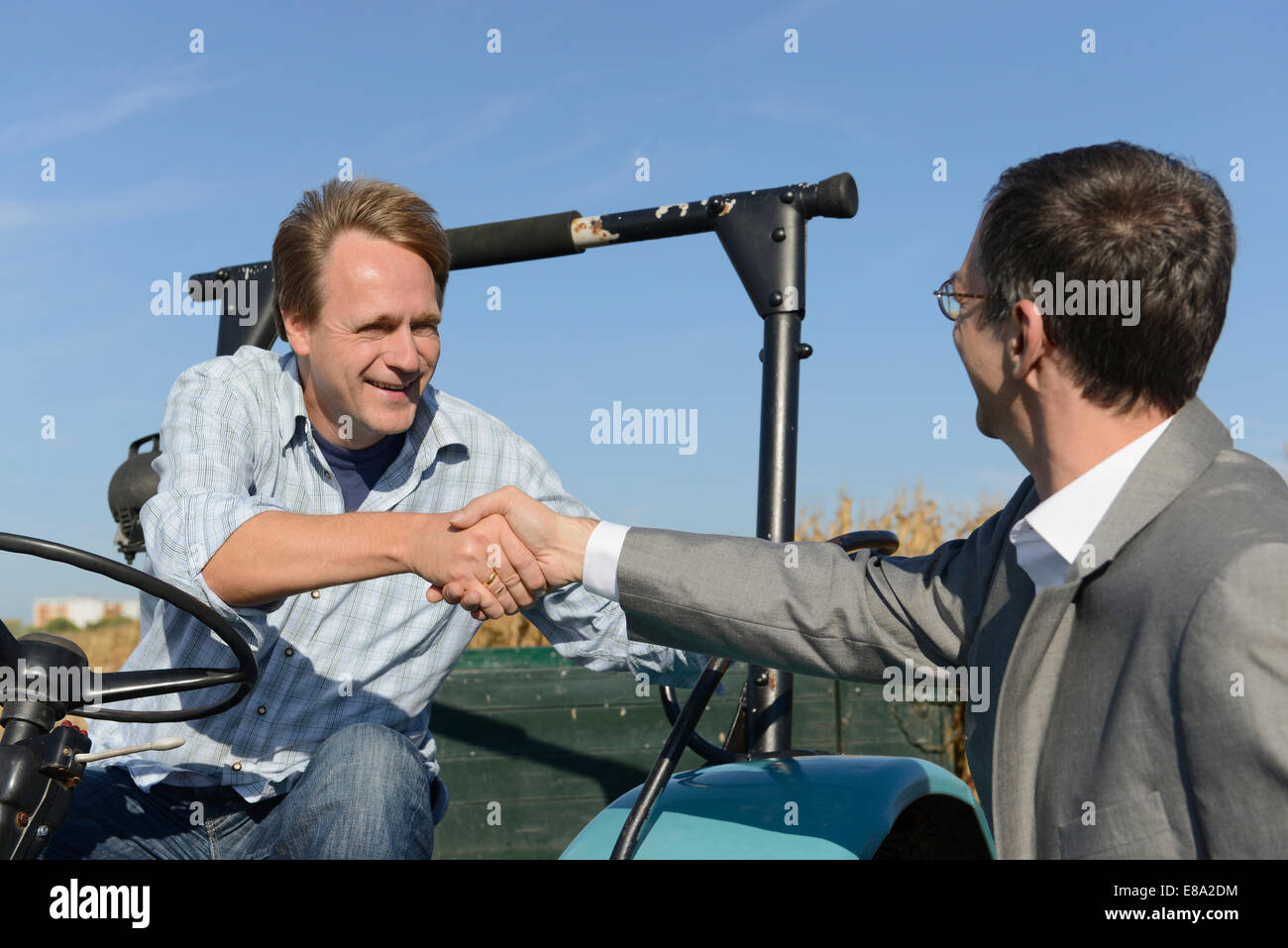 Farmer welcomes businessman with handshake while sitting on a tractor ...