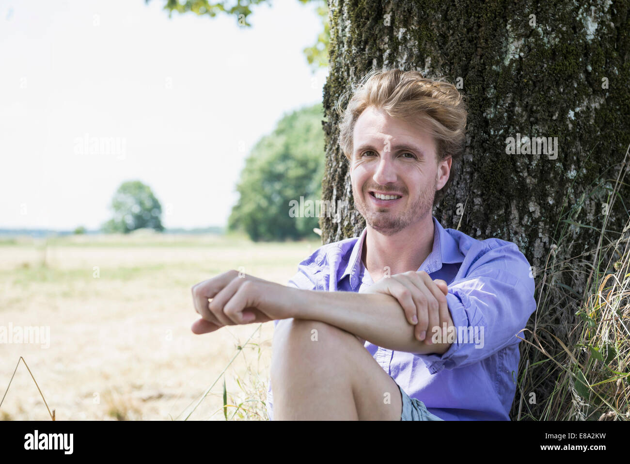 Portrait of mid adult man sitting under tree, smiling Stock Photo - Alamy