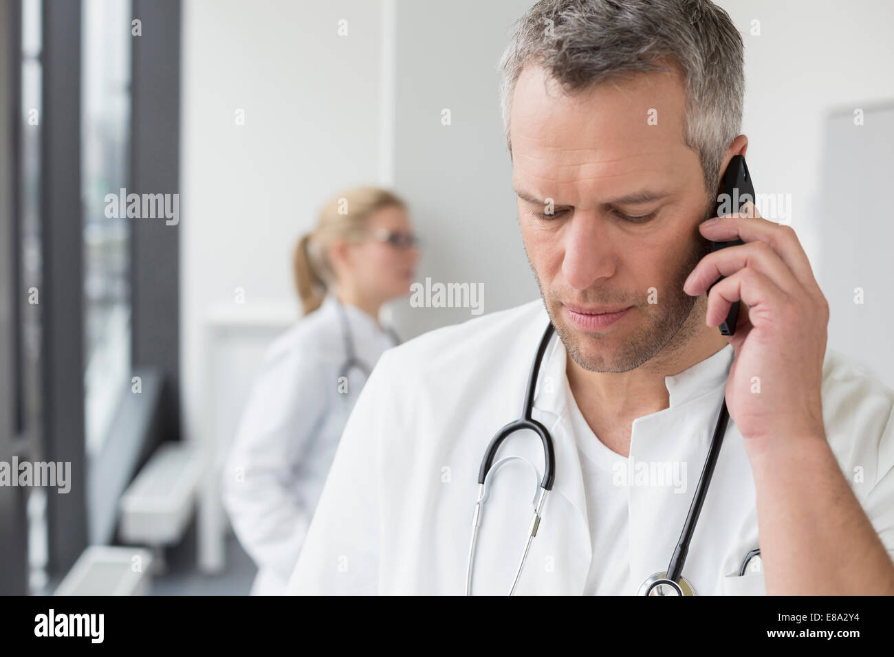 Doctor on phone while female doctor in background Stock Photo - Alamy