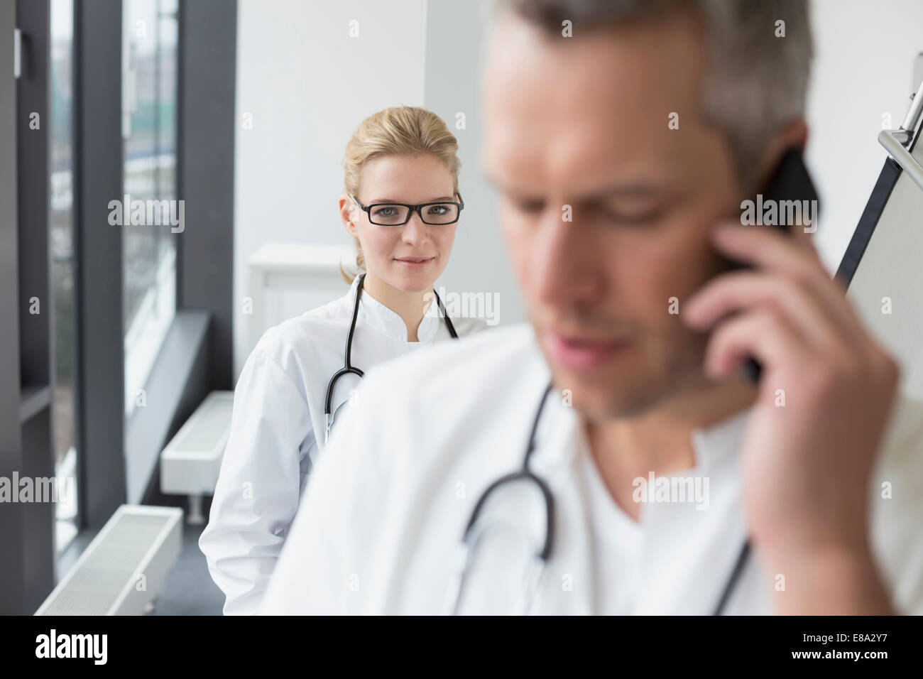 Doctor on phone while female doctor in background Stock Photo - Alamy