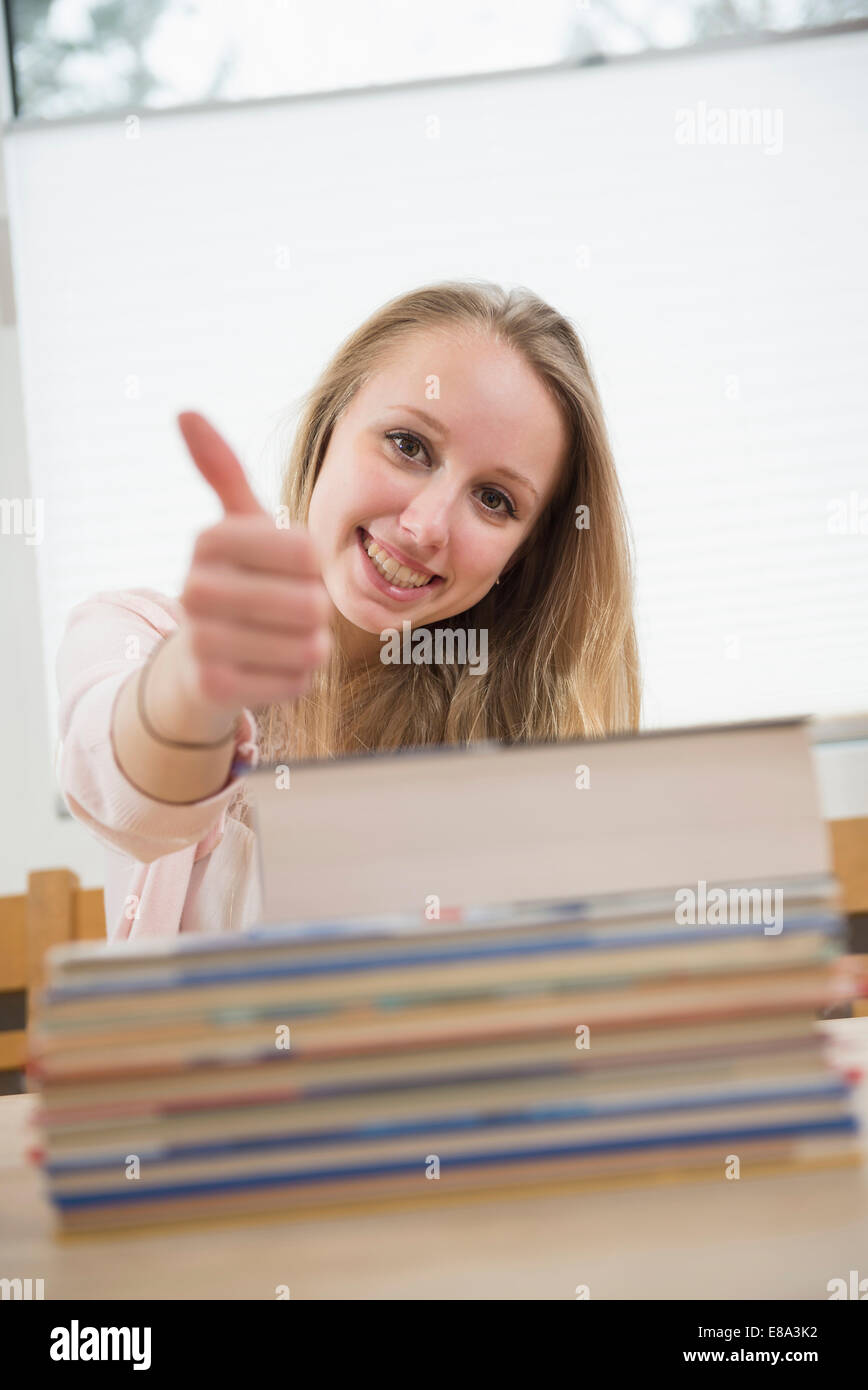 Portrait of teenage girl with books and showing thumbs up, smiling ...