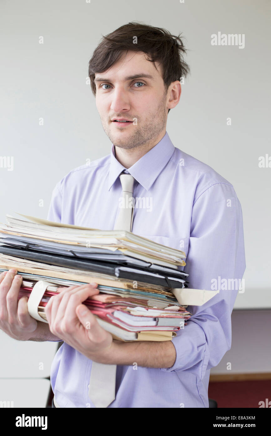 Portrait of businessman holding stack of files in office, smiling Stock ...