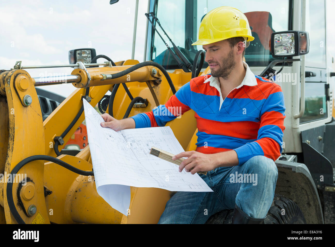 Construction worker sitting on excavator holding construction plan ...