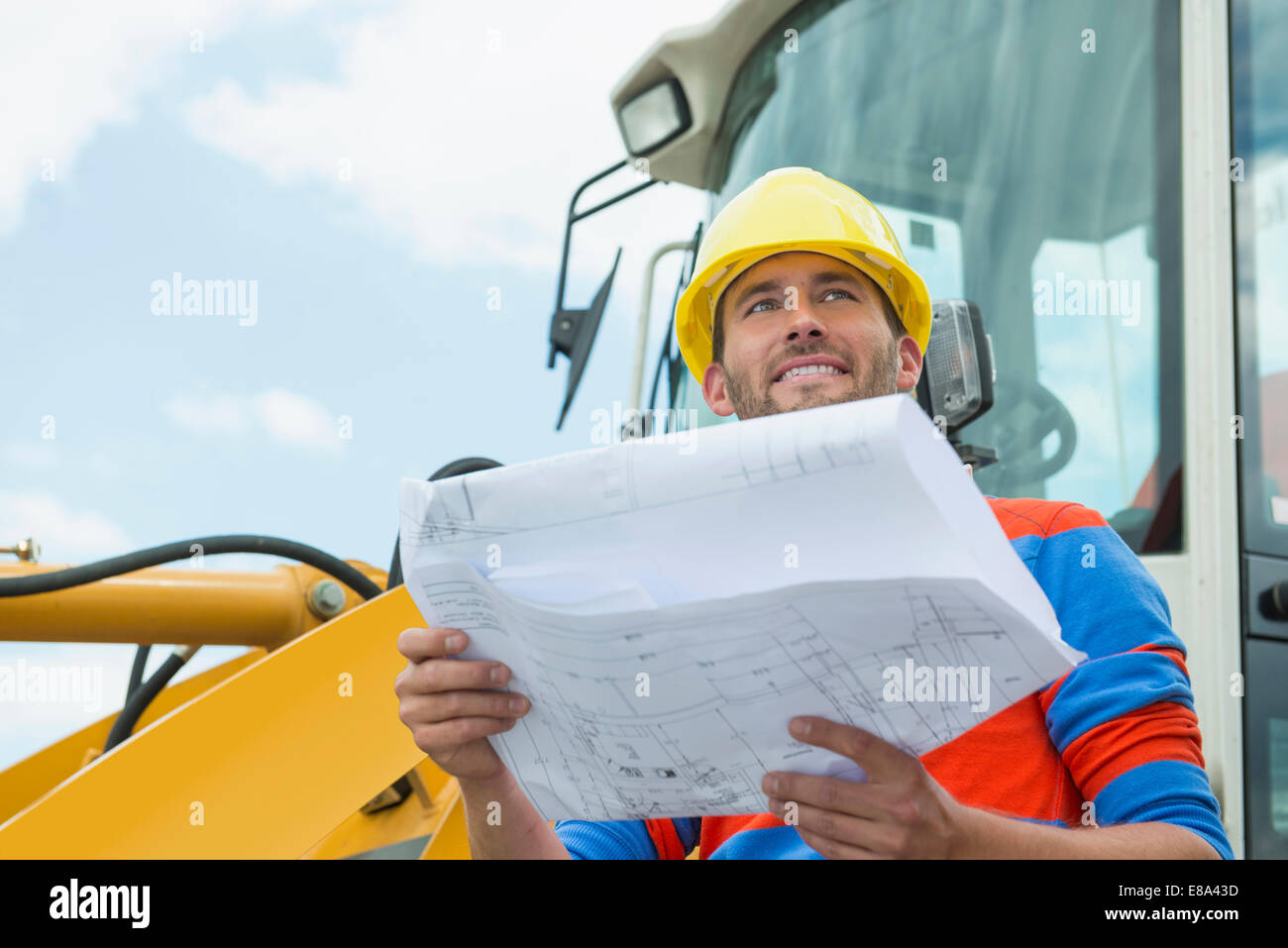 Construction worker holding construction plan in front of excavator ...