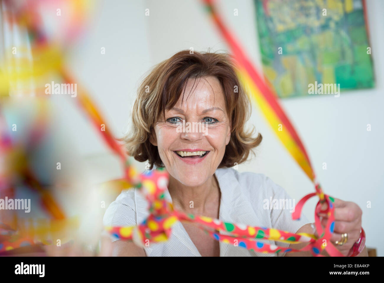 Portrait of senior woman with blowout paper streamer, smiling Stock ...