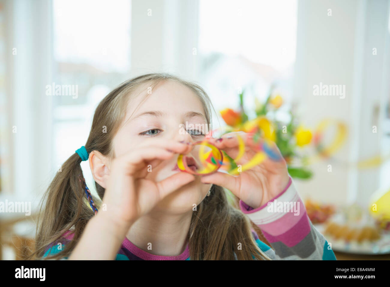 Portrait of girl with blowout paper streamer at birthday party, smiling ...