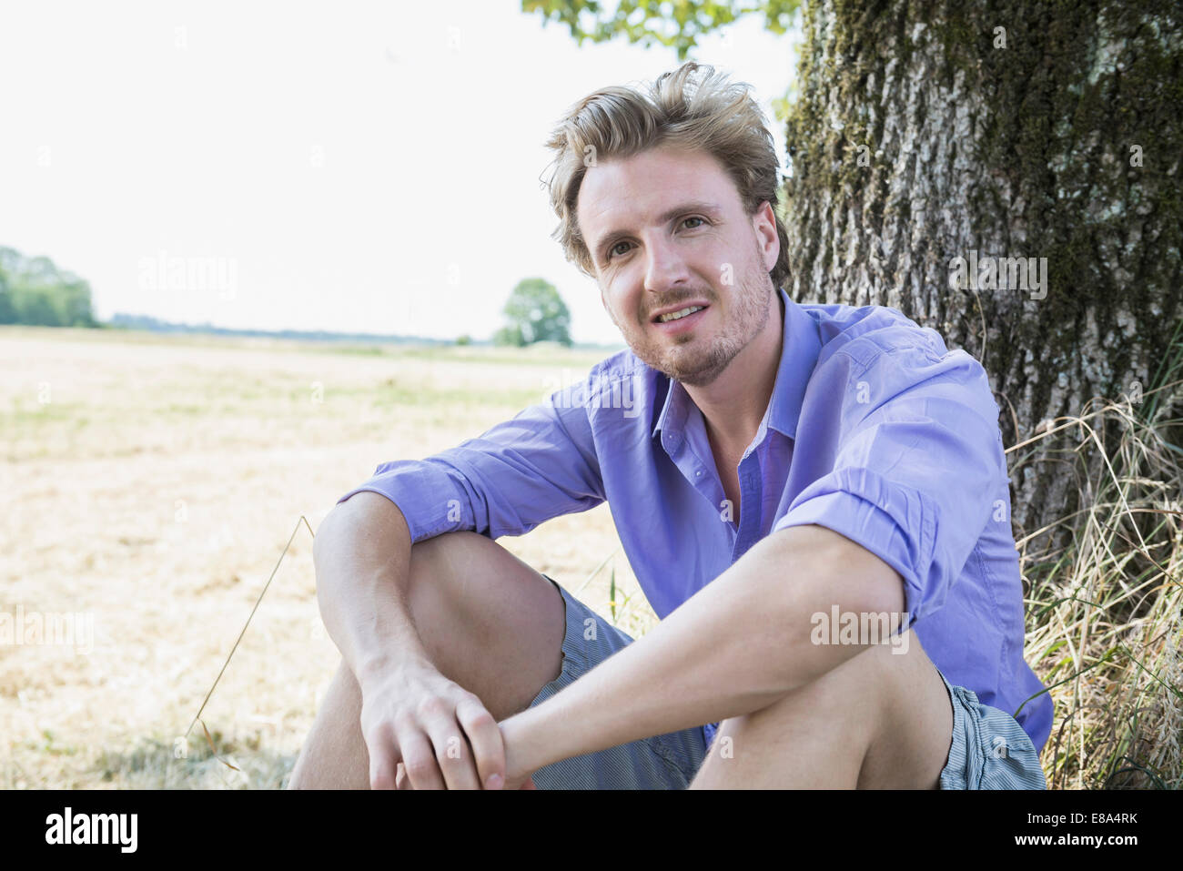 Portrait of mid adult man sitting under tree, smiling Stock Photo - Alamy